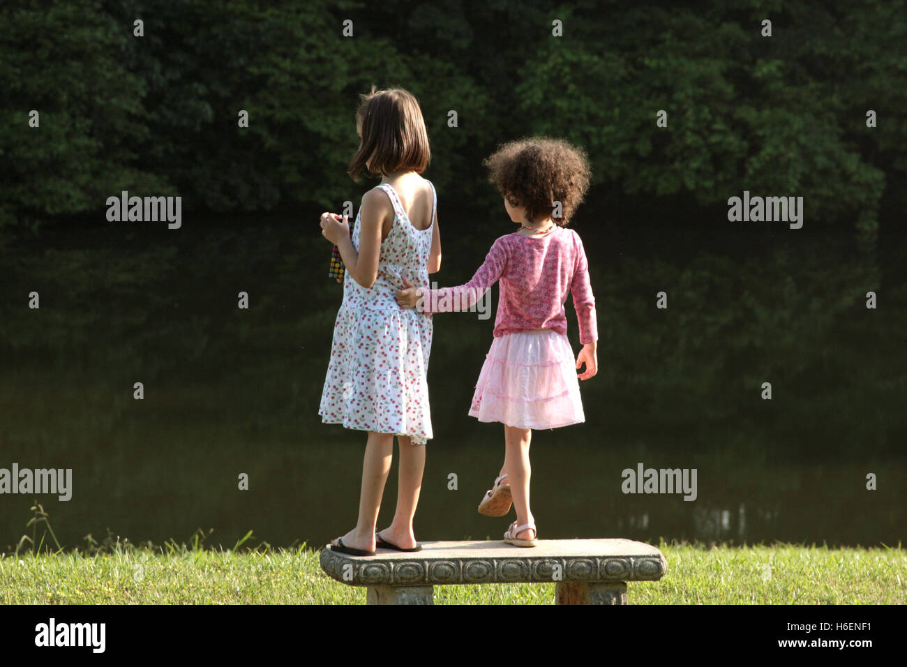 Two little girls standing on stone bench looking towards a lake Stock ...