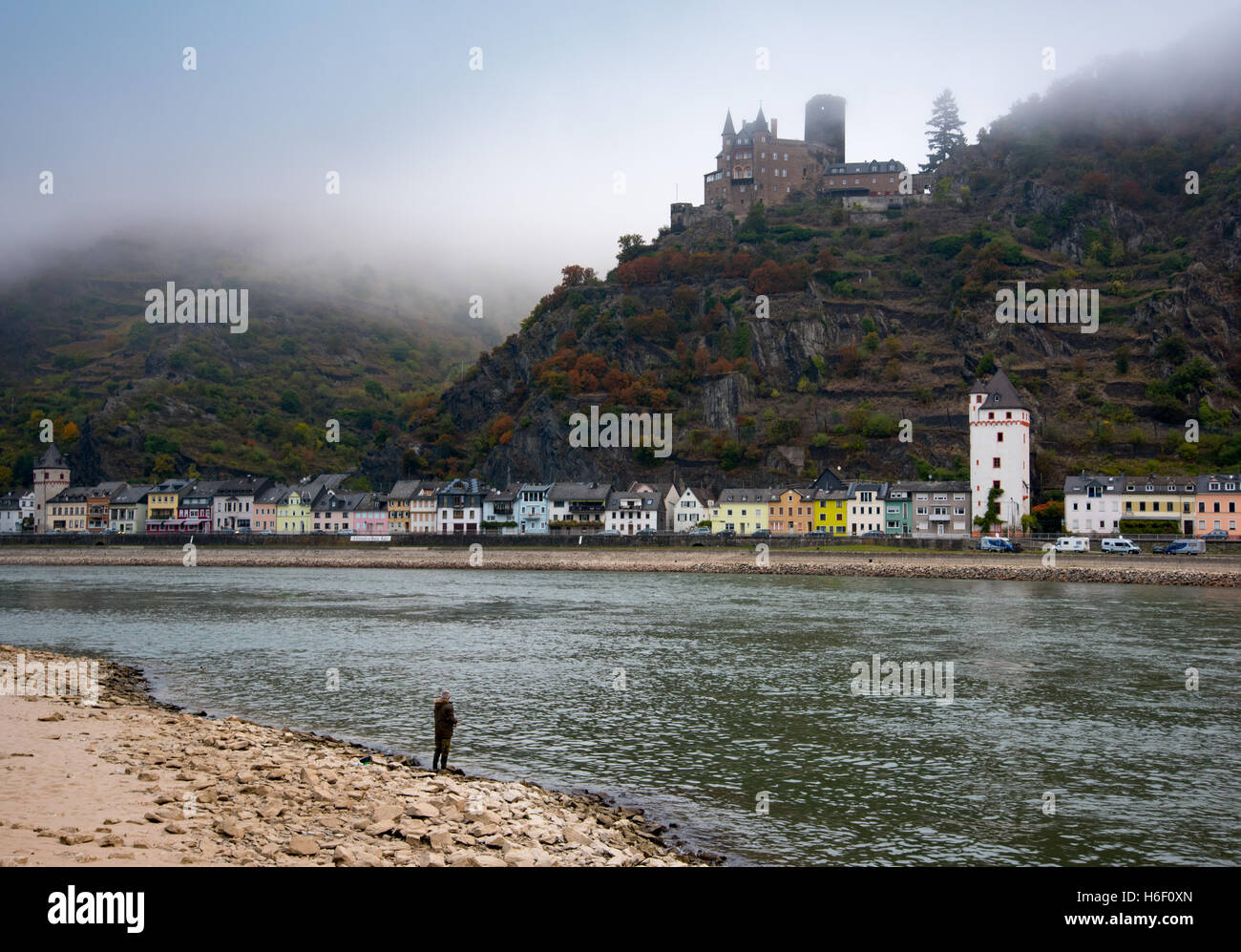 Lone man on bank of Rhine opposite Burg Katz castle in morning mist, St ...