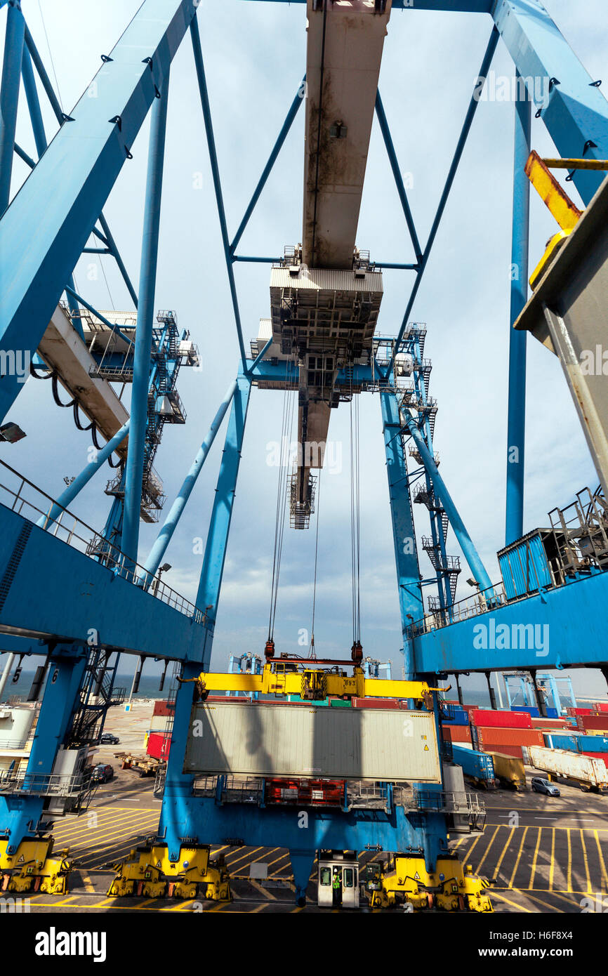 A massive freight crane transports a container from a truck onto a ...