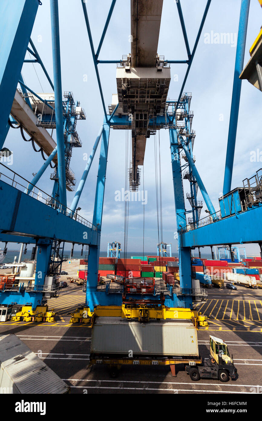 A massive freight crane transports a container from a truck onto a ...