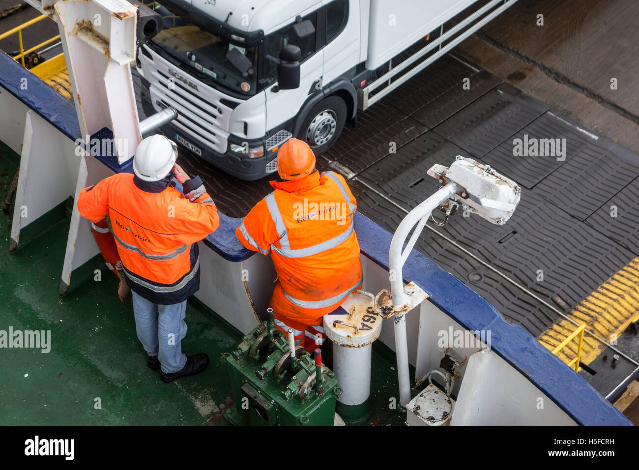 Ship's crew members in orange workwear watching trucks boarding ferry ...