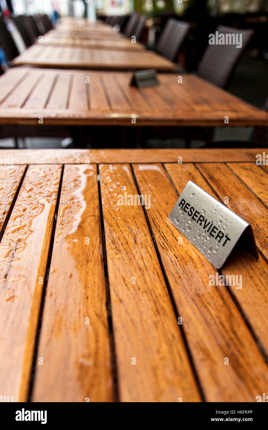 A row of cafe tables wet from the rain, with a sign saying "reserved ...