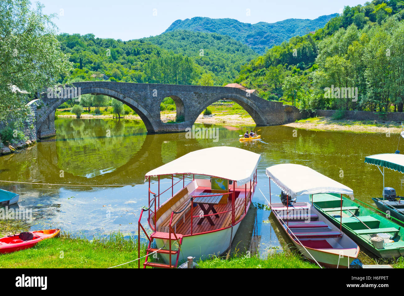 The stone arch bridge in Rijeka Crnojevica with the tourist boats, moored at the bank of ...