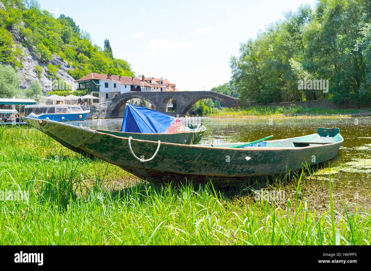 The old wooden boat with the medieval stone bridge on the background, Rijeka Crnojevica ...