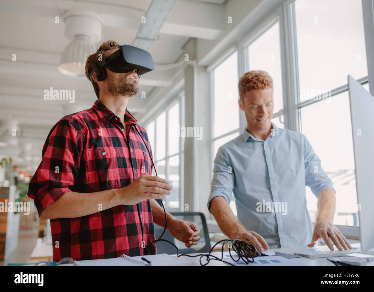Young developer working on laptop and virtual reality glasses. Two men improving virtual reality ...
