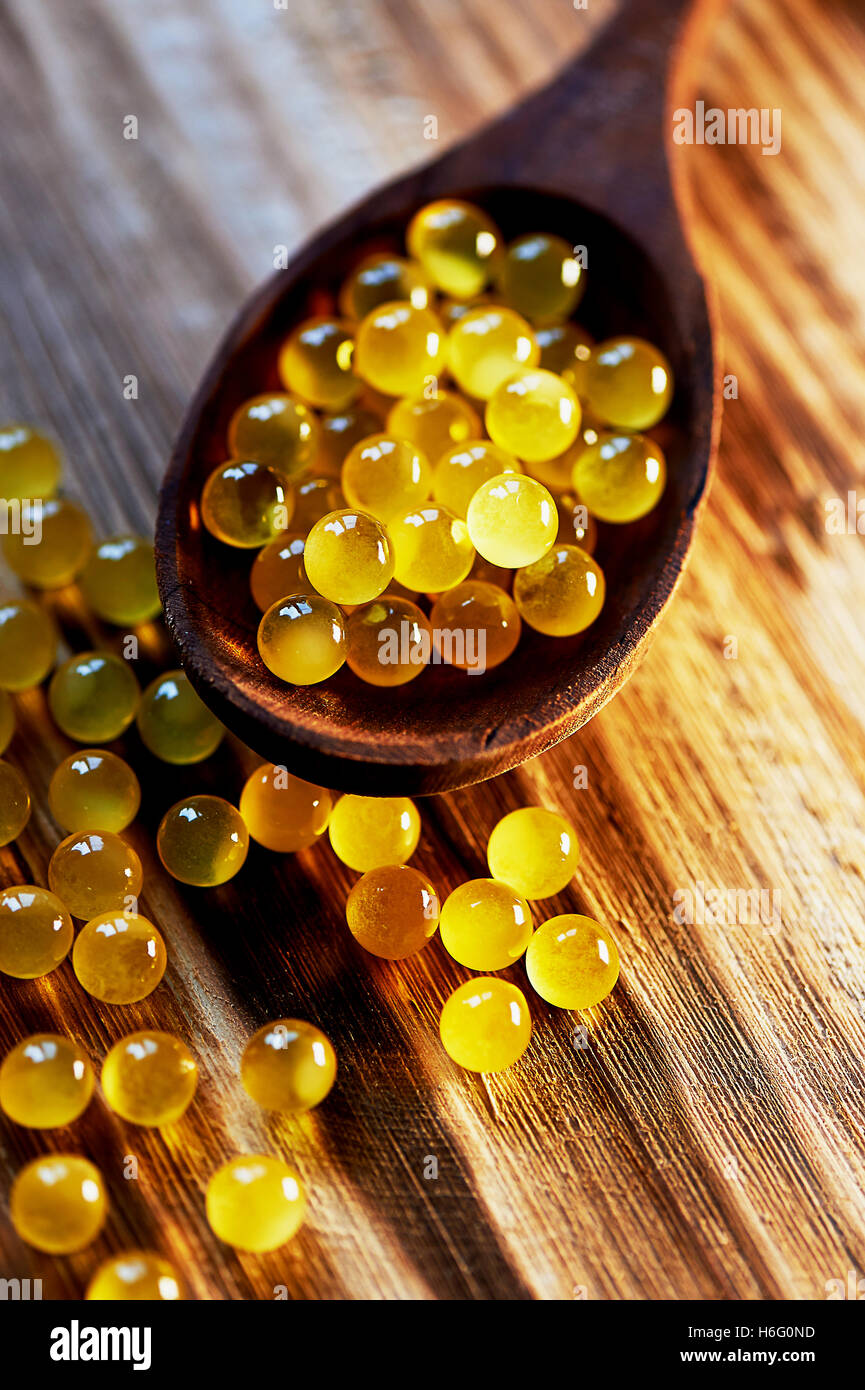 Round small fish oil capsules on wooden spoon scattered on a wooden ...