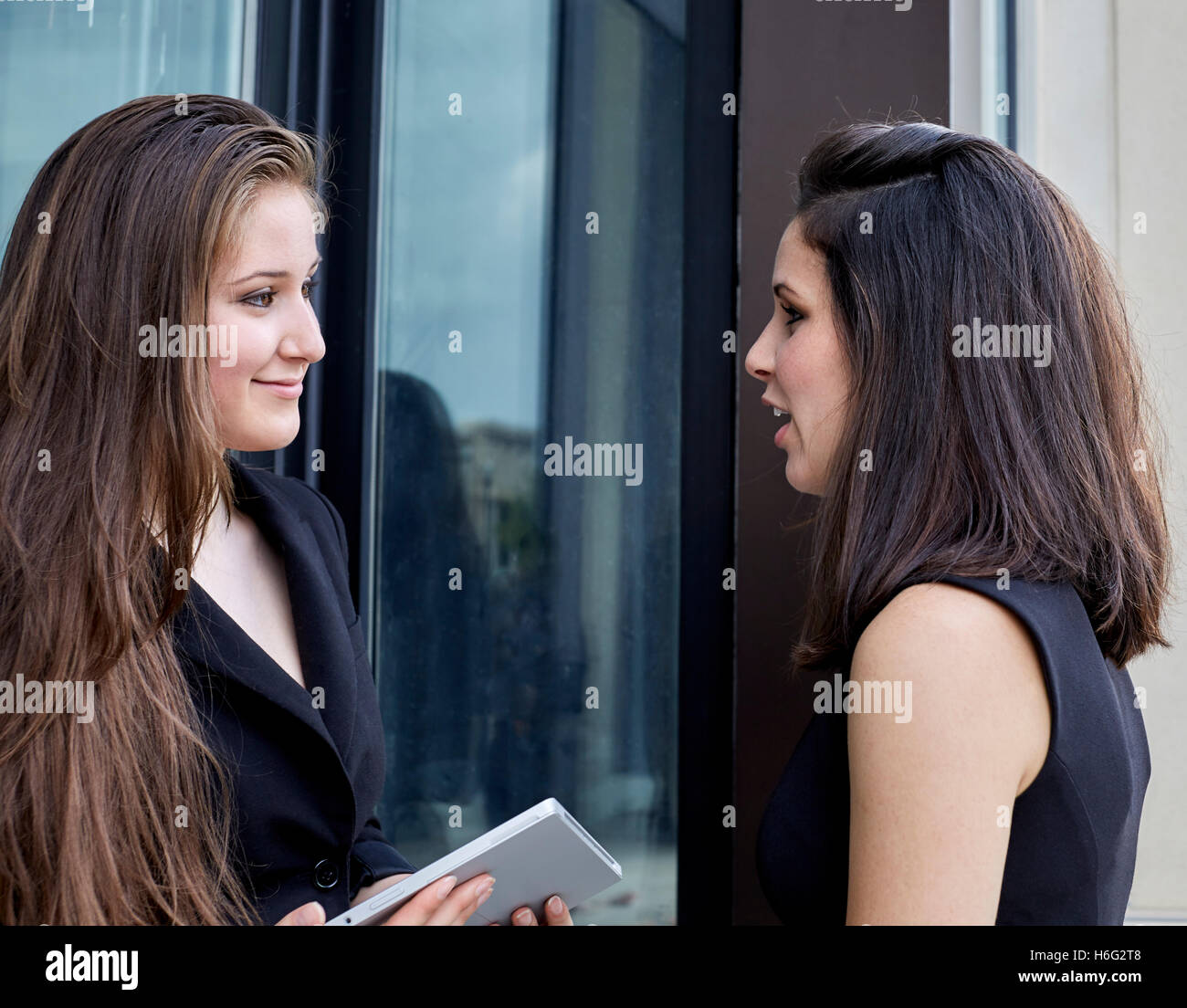 Two young career women having a conversation outside an office building ...