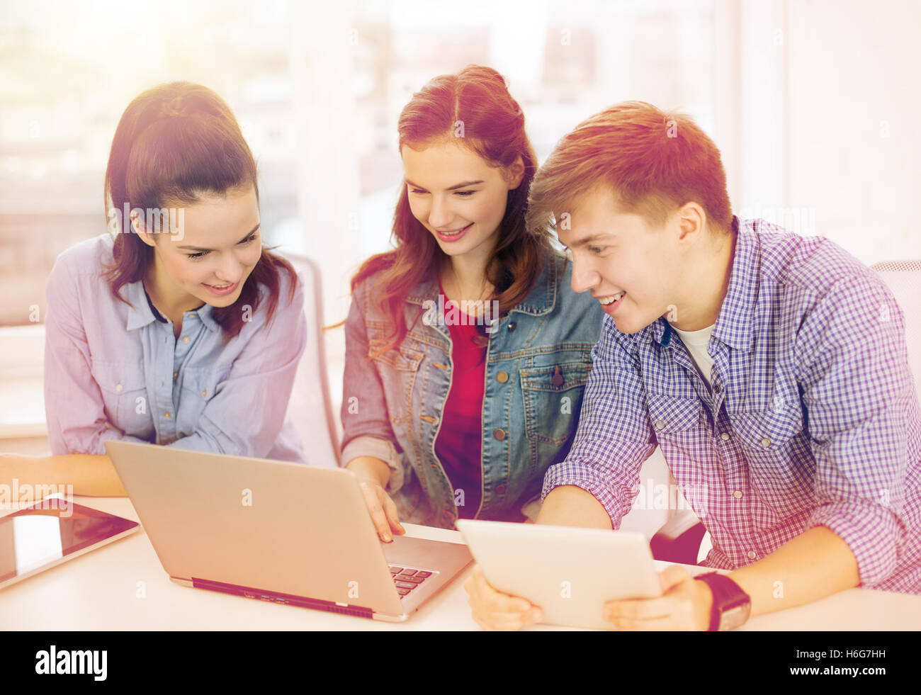 three smiling students with laptop and tablet pc Stock Photo - Alamy
