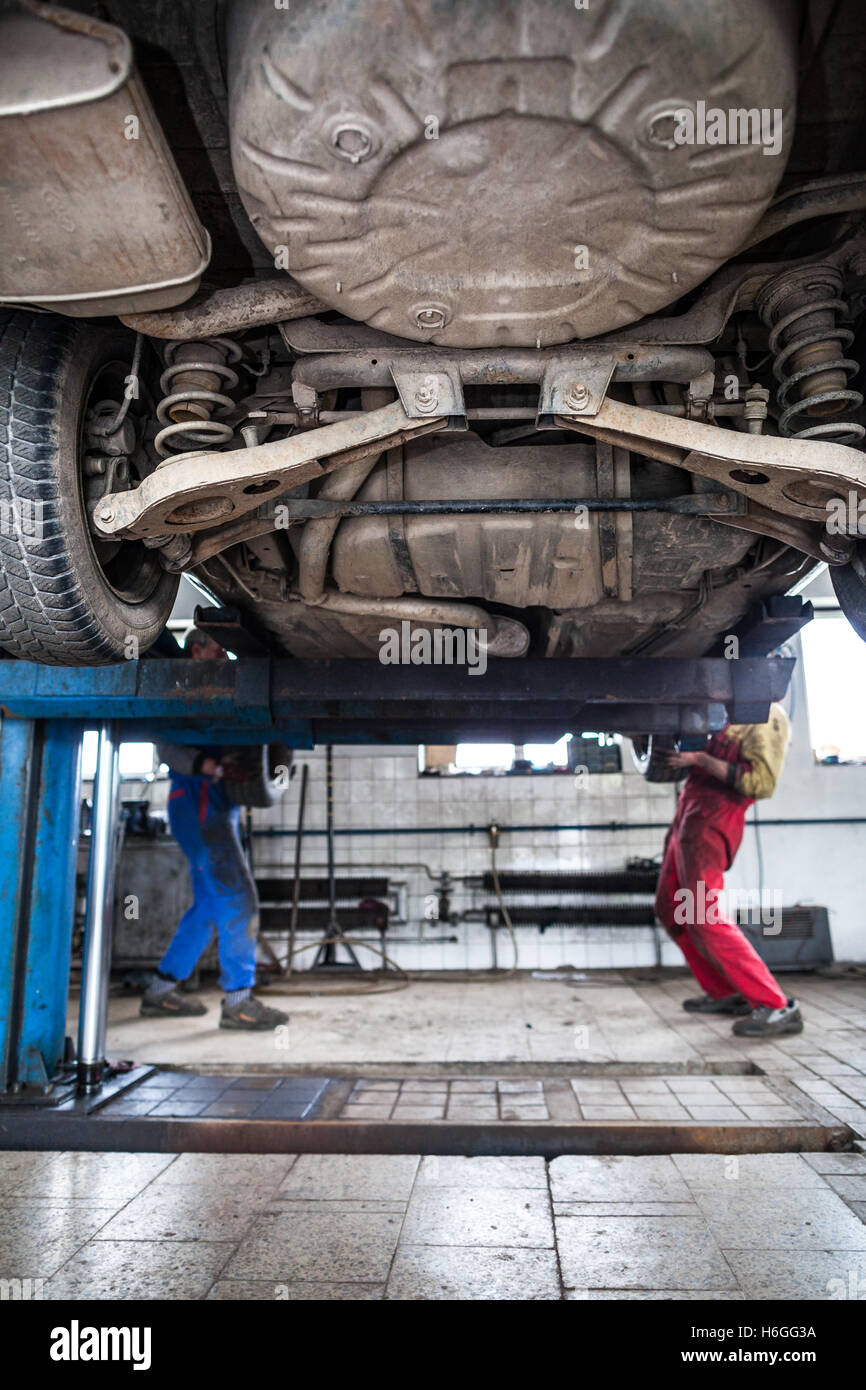 inside a garage - two mechanics working on a car, changing wheels ...