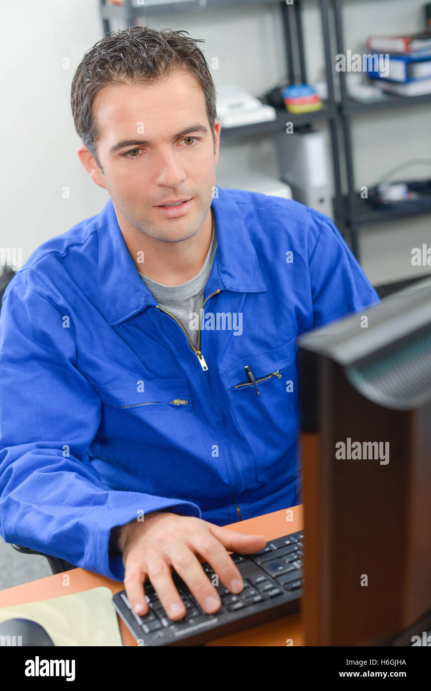 Man in blue overalls sat at his desk Stock Photo - Alamy