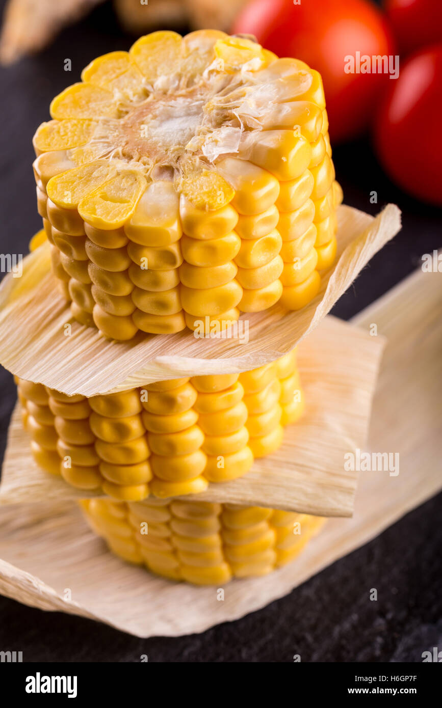 Vertical photo of three pieces of yellow sweet corn. Food is placed on ...