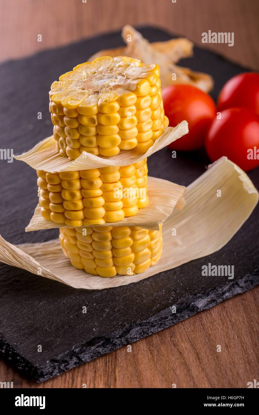 Vertical photo of three pieces of yellow sweet corn. Food is placed on ...
