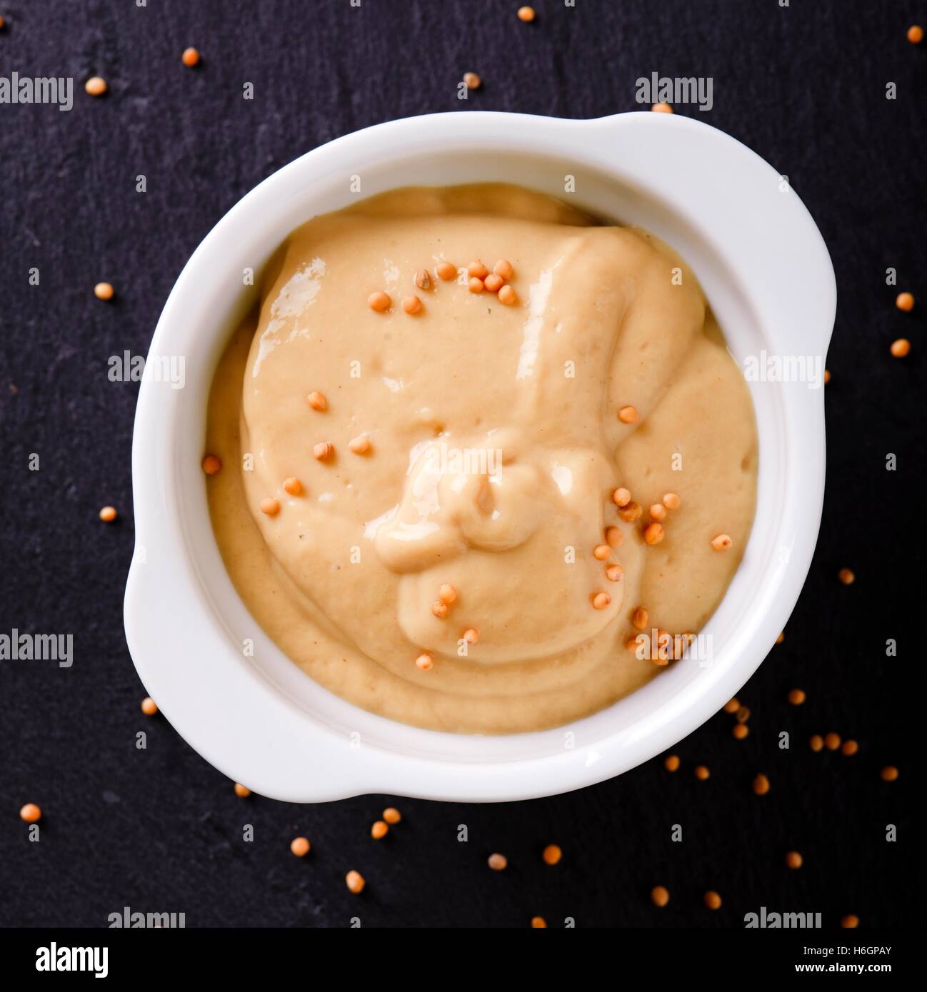 Square photo of bowl with mustard. White oval bowel full of orange ...