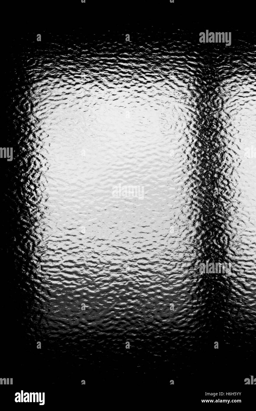 The silhouette of a window as seen through a glass with a bumpy surface ...