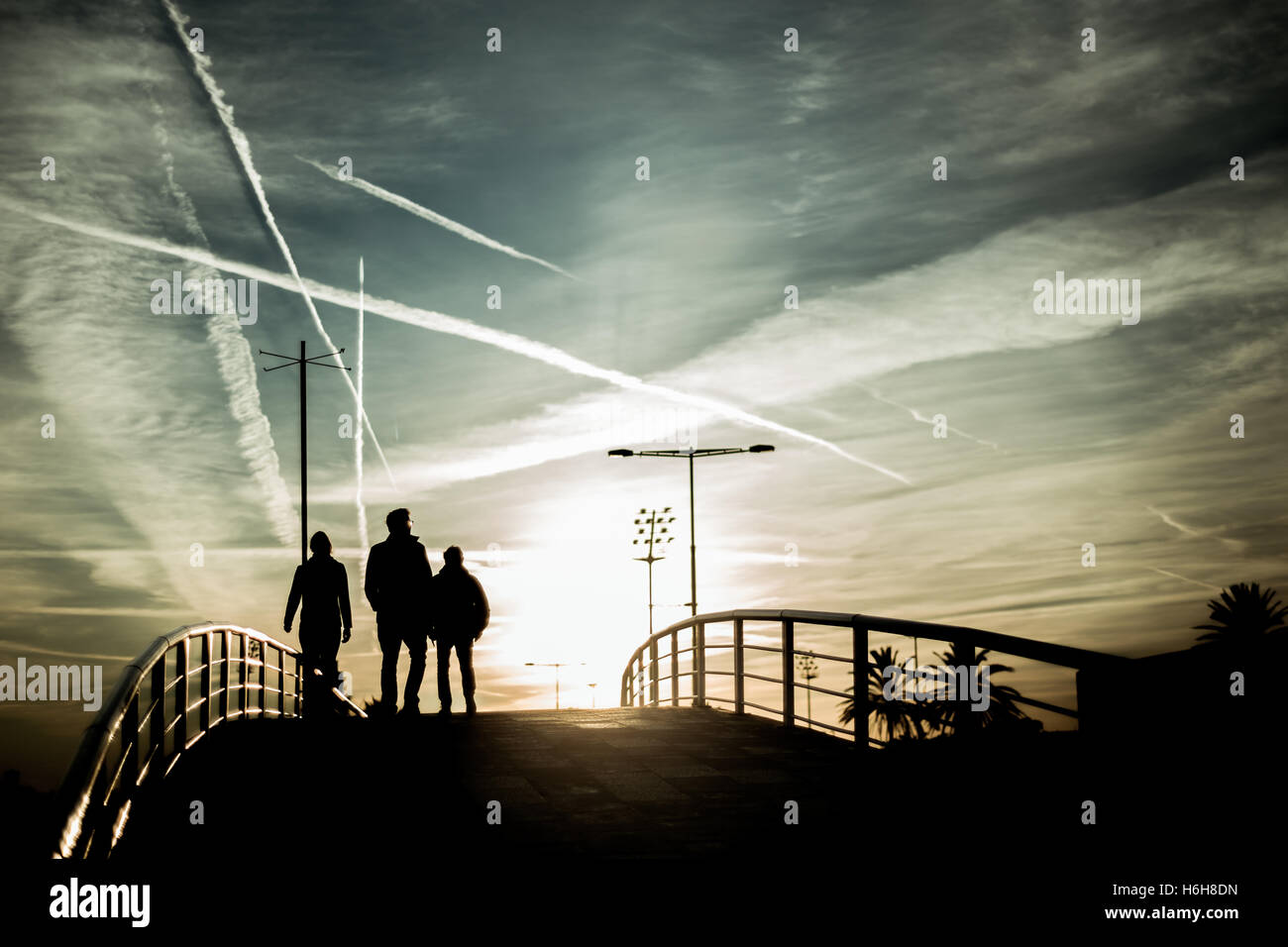 Three human silhouettes crossing the bridge. Backlight with beautiful ...