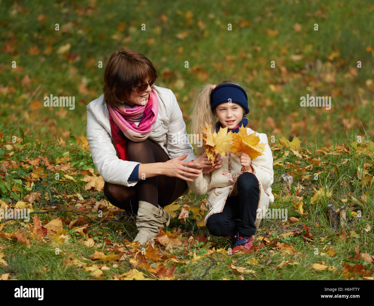 Mother and daughter are playing with autumn leaves. They are surrounded ...