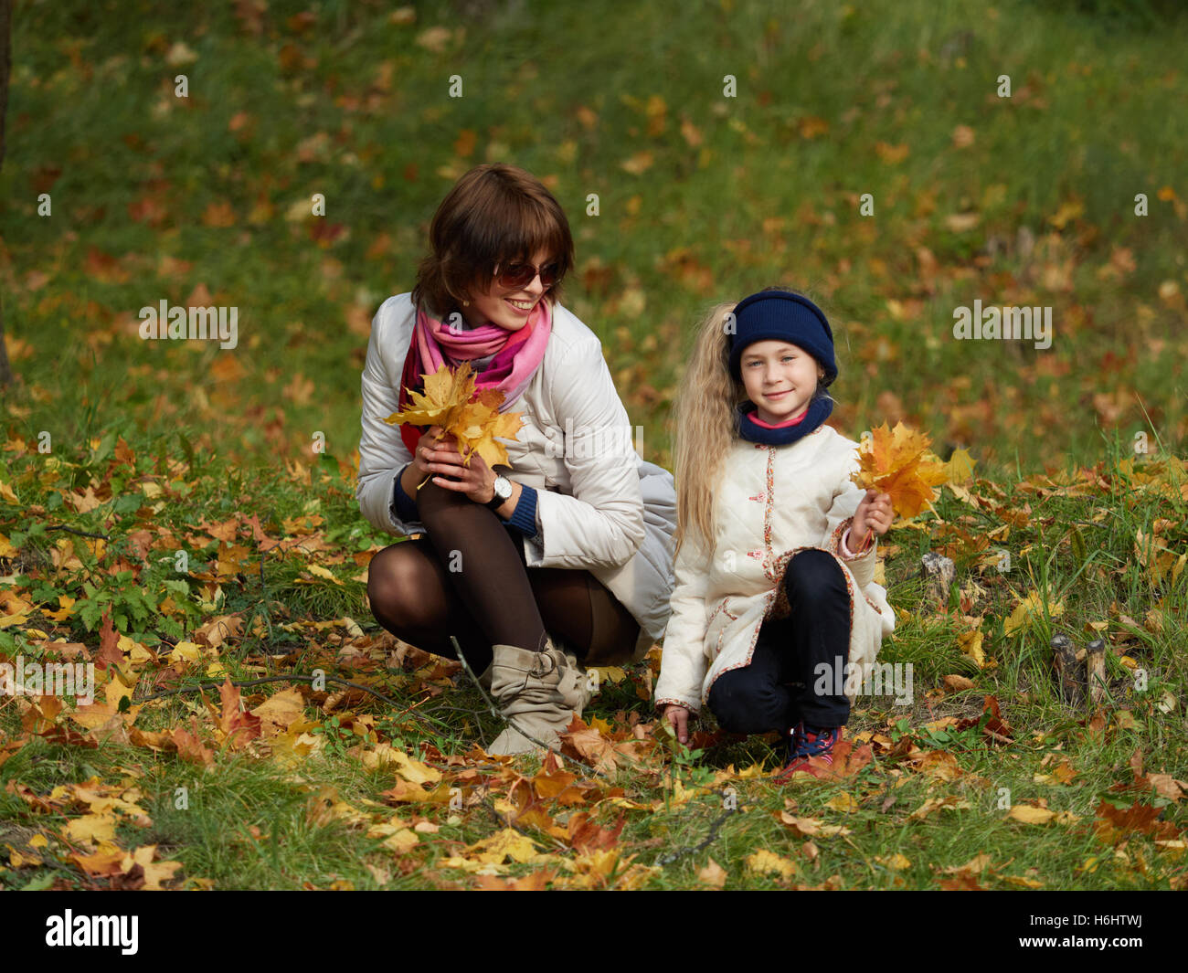 Mother and daughter are playing with autumn leaves. They are surrounded ...