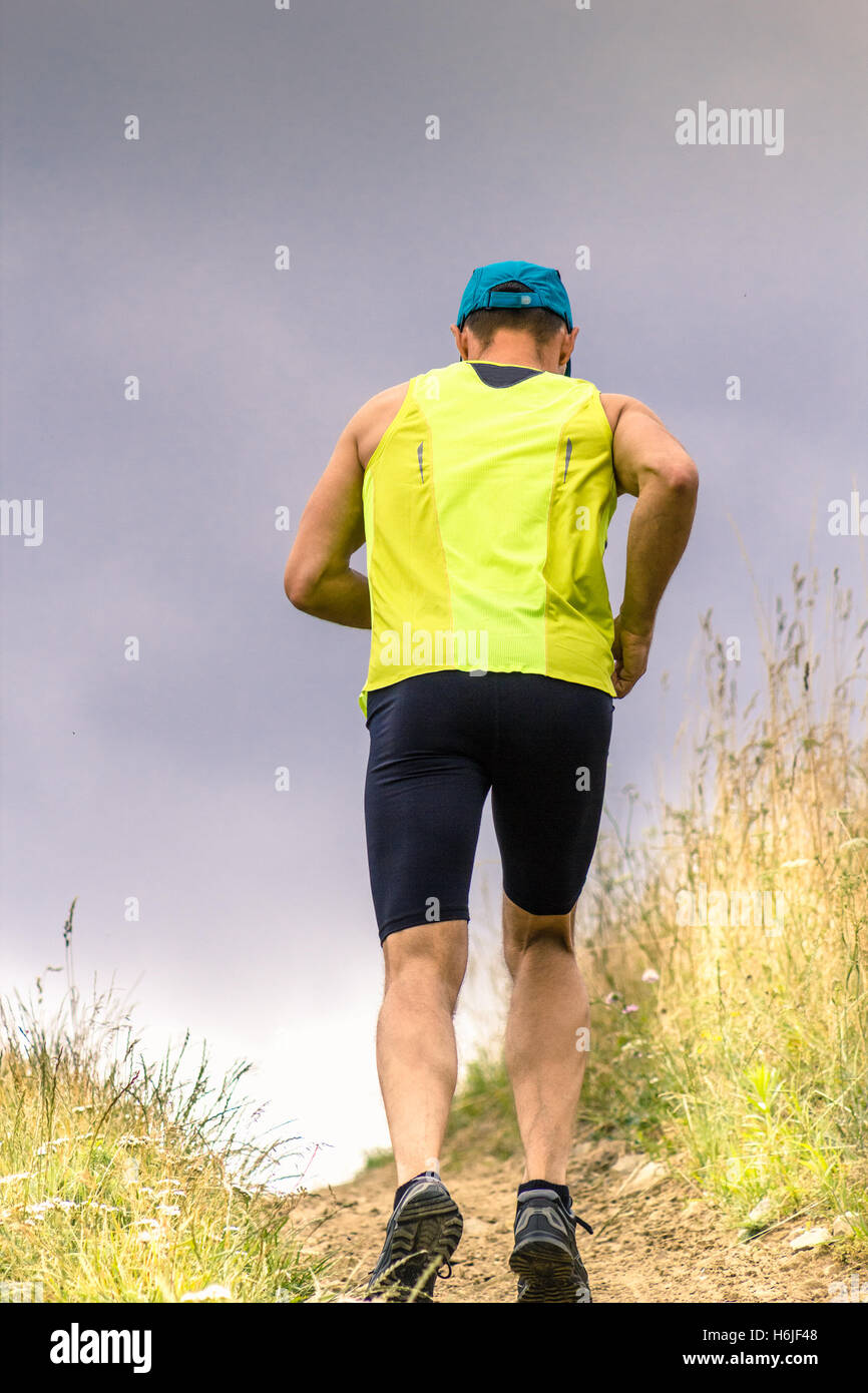 Athletic male runner running uphill on dirt road. Low angle back view ...