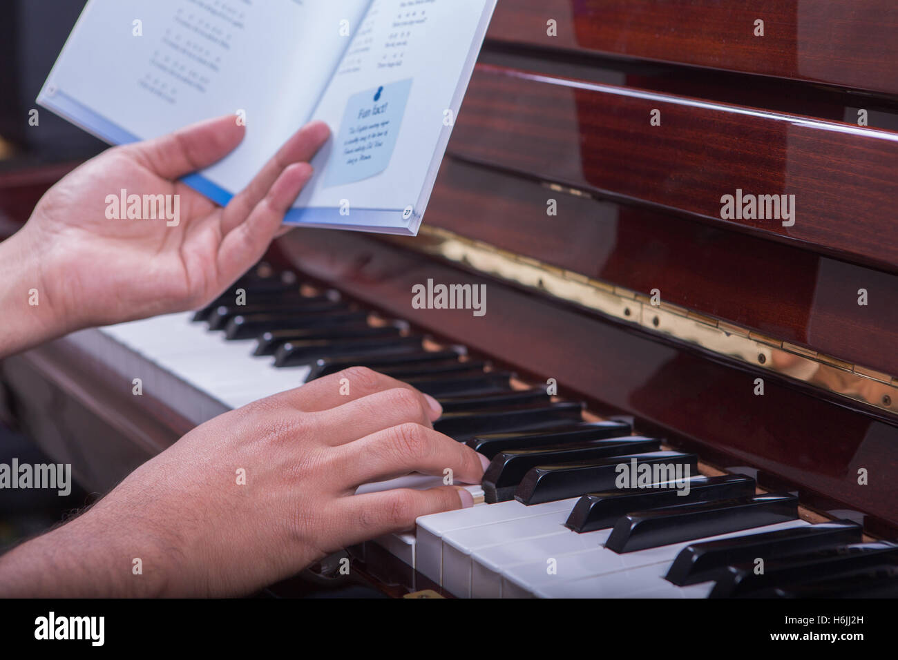 Man playing on a piano from a book holding in left hand Stock Photo - Alamy