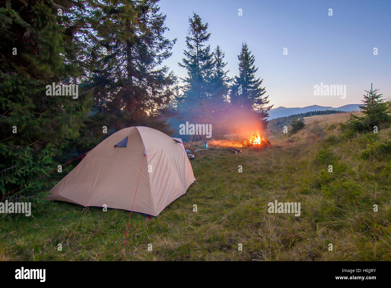 Hikers tent in mountains at evening with a bonfire with sparkles near ...