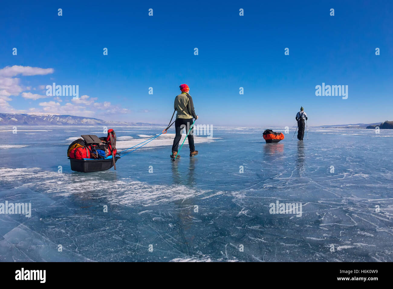 a woman and a man with a sledge and trekking pole is on the blue ice of ...