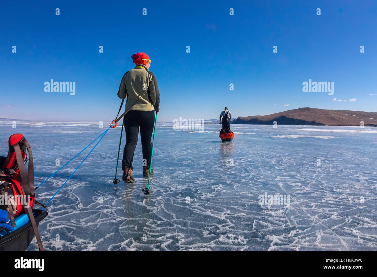 a woman and a man with a sledge and trekking pole is on the blue ice of ...