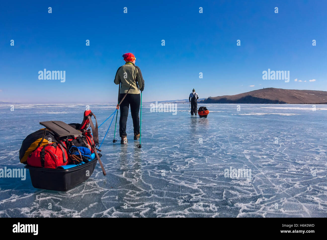 a woman and a man with a sledge and trekking pole is on the blue ice of ...