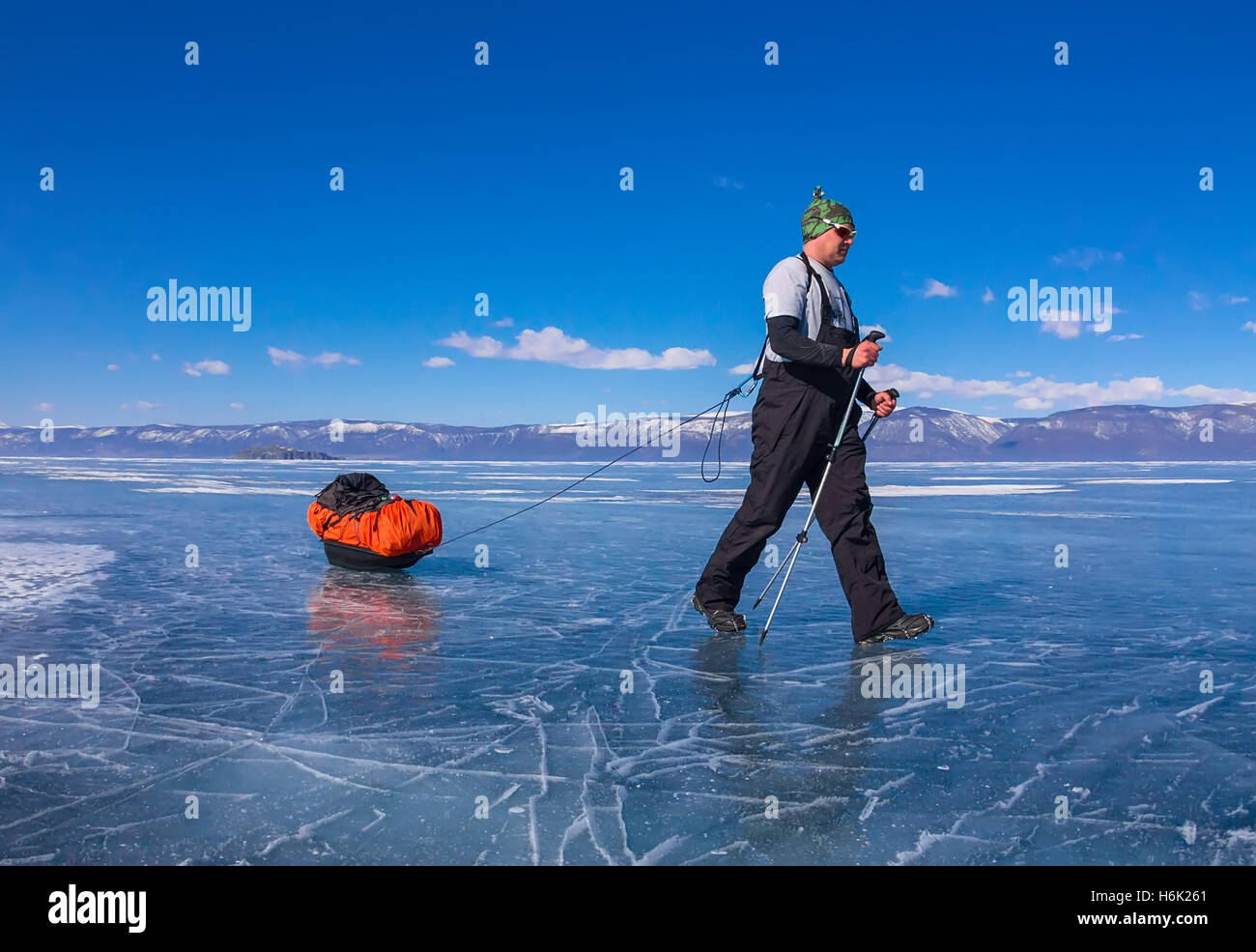 Man with a sledge and trekking pole is on the ice of Lake Baikal Stock ...