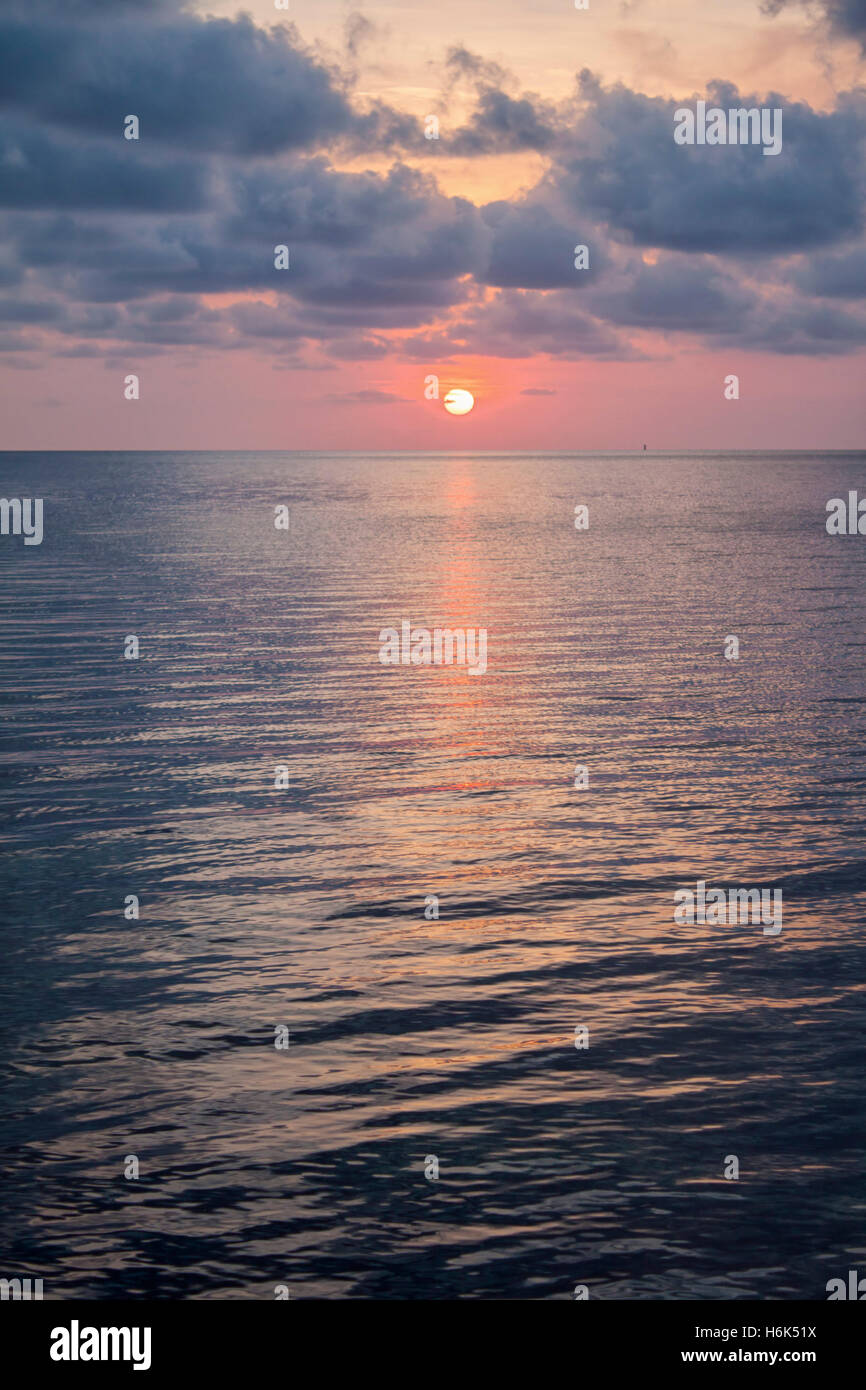 sun setting into the ocean on a cloudy day Stock Photo - Alamy