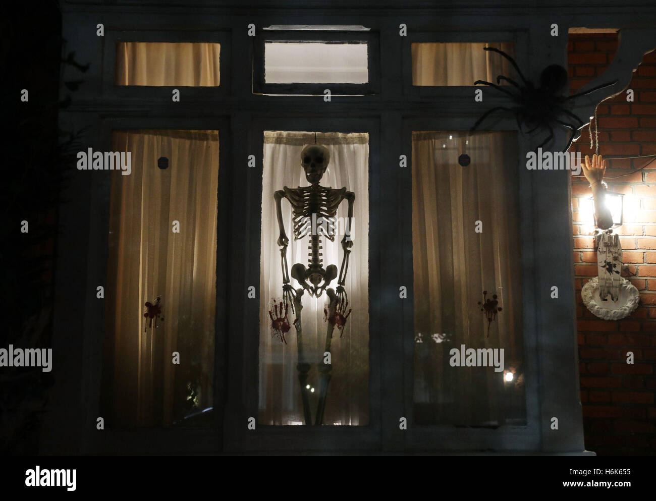 A Halloween-themed skeleton decoration hangs in the window of a house ...