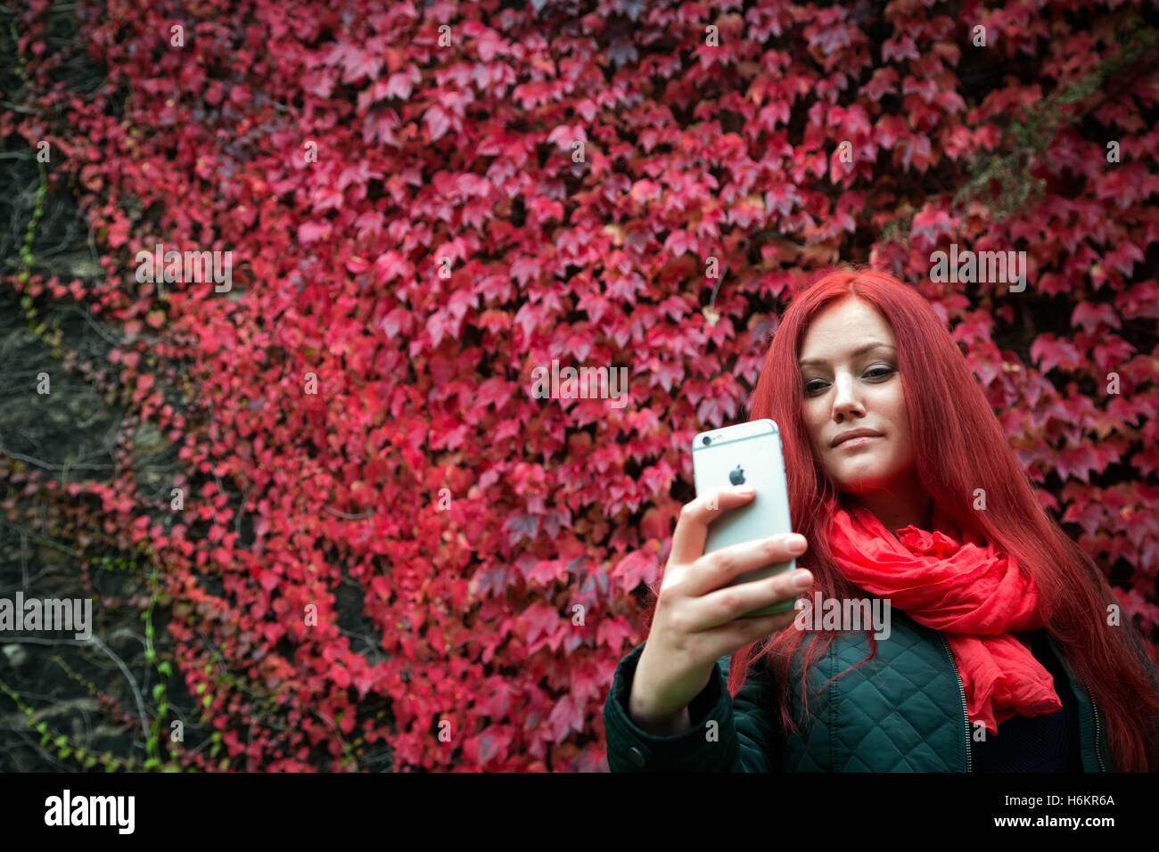 A red headed women takes a photo-selfie of the intense autumn red ...