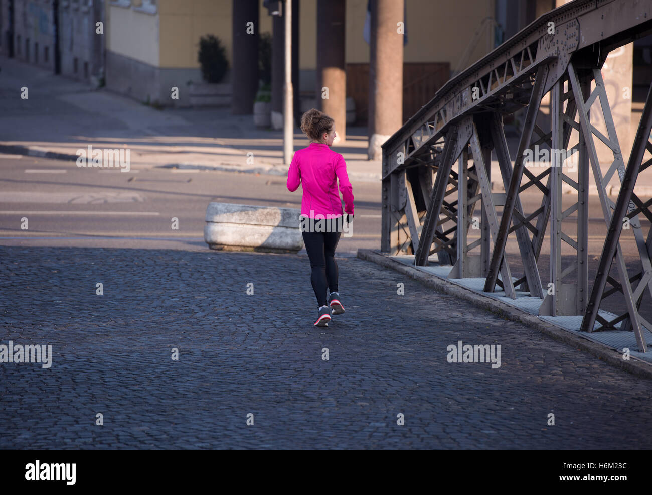 sporty woman running on sidewalk at early morning jogging with city ...