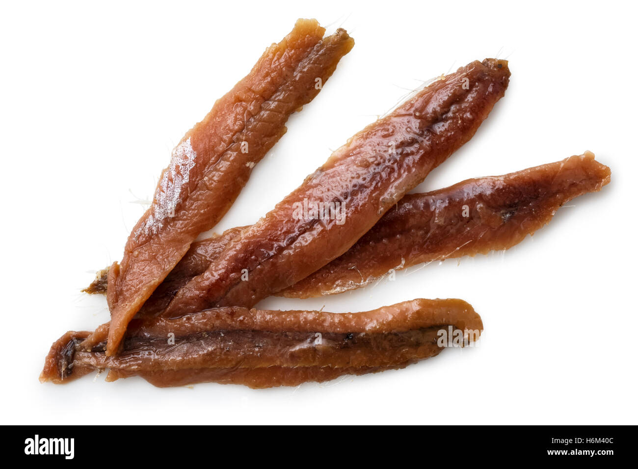 Four anchovy fillets with oil arranged and isolated on white from above ...
