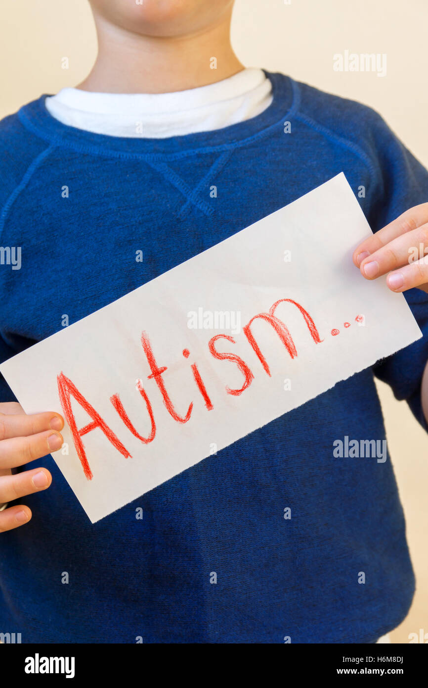 Young boy (children hands) hold Autism text written on sheet of paper ...