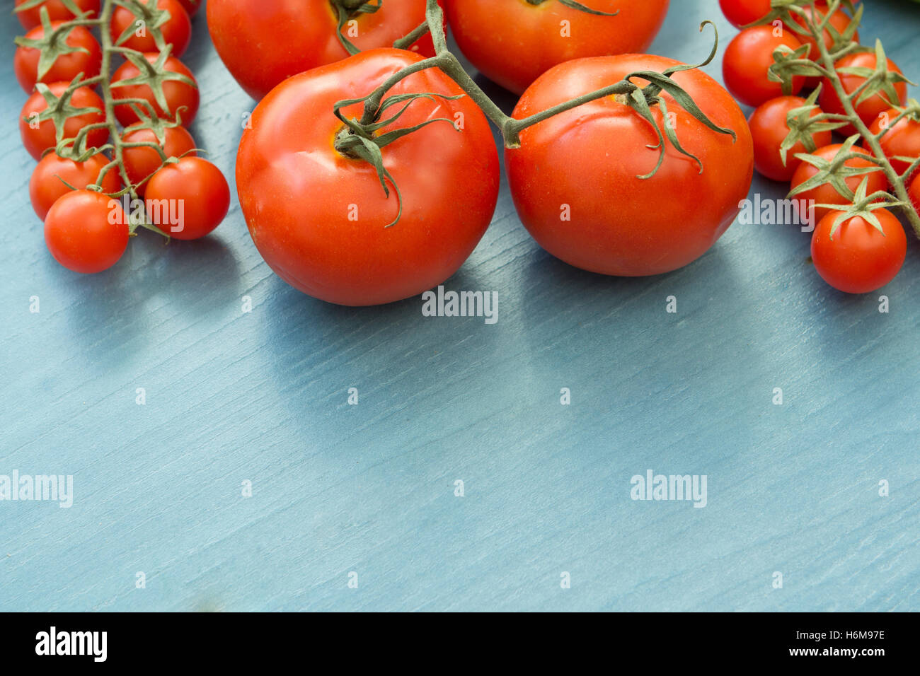 Differents size of tomatoes with leaf on a blue wooden surface Stock ...