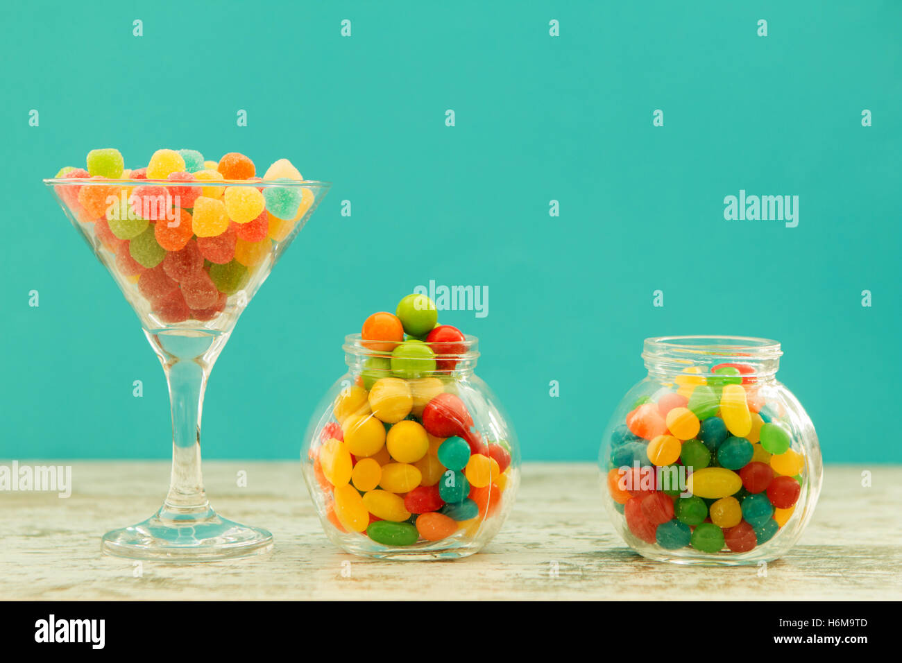 Three glass jars full of jellybeans on wooden table with blue ...