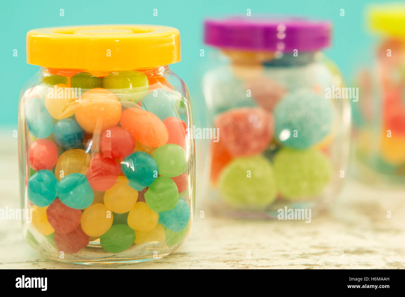 Three glass jars full of jellybeans on wooden table with blue ...