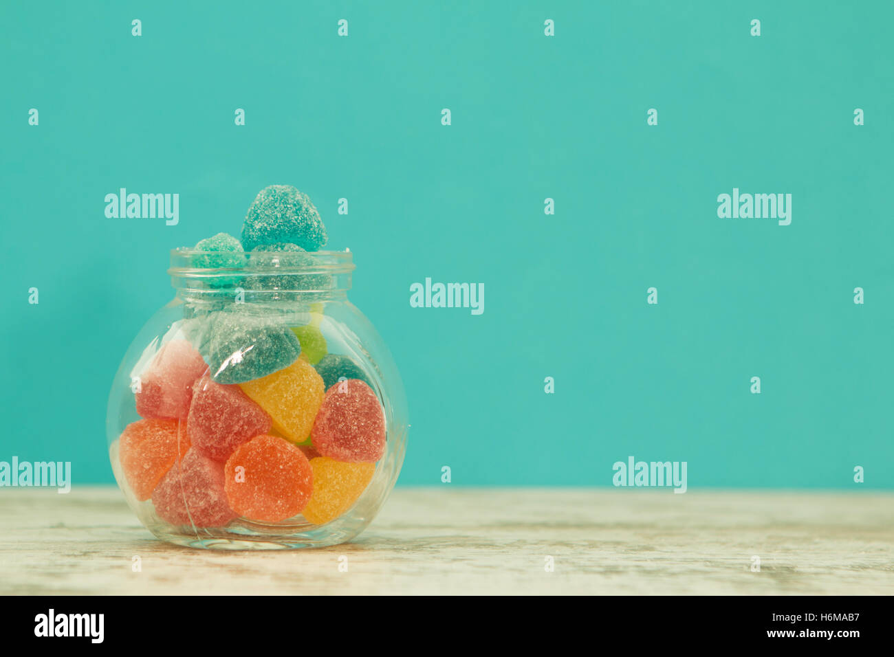 Glass jar full of jelly beans on a wooden table with blue background ...