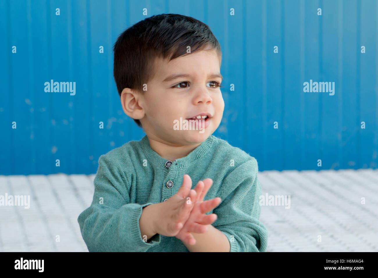 Cheerful child playing palms on the street in front of a blue wall ...