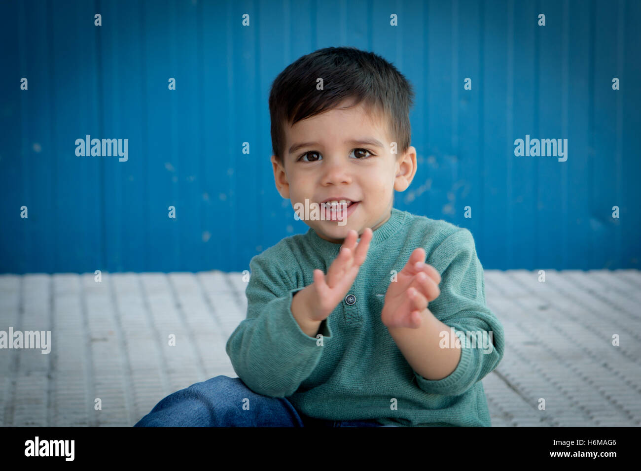 Cheerful child playing palms on the street in front of a blue wall ...
