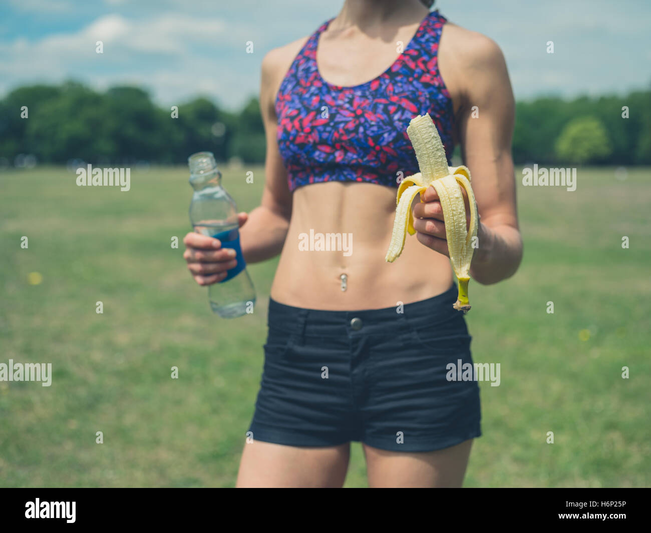 A fit and athletic young woman is standing in the park with a banana ...