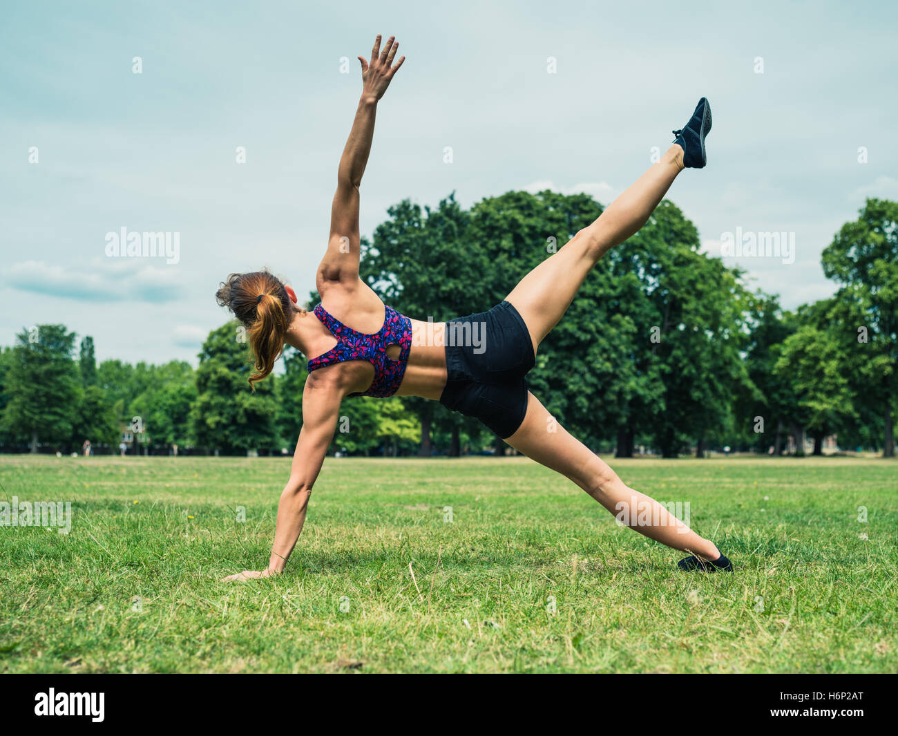 A fit and athletic young woman is working out in a park and is doing a ...