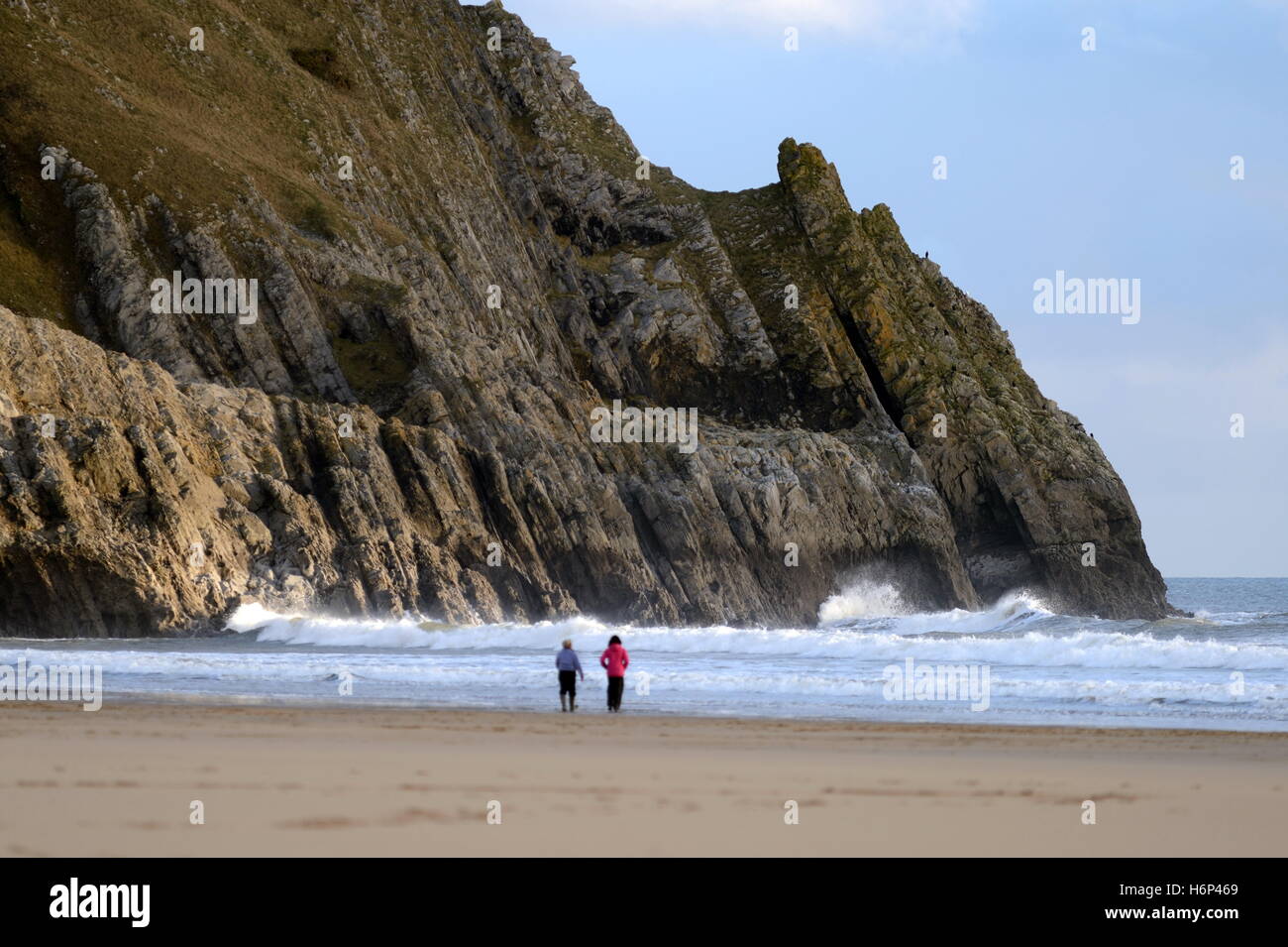 2 people on the beach with surf breaking against the cliffs that plunge ...