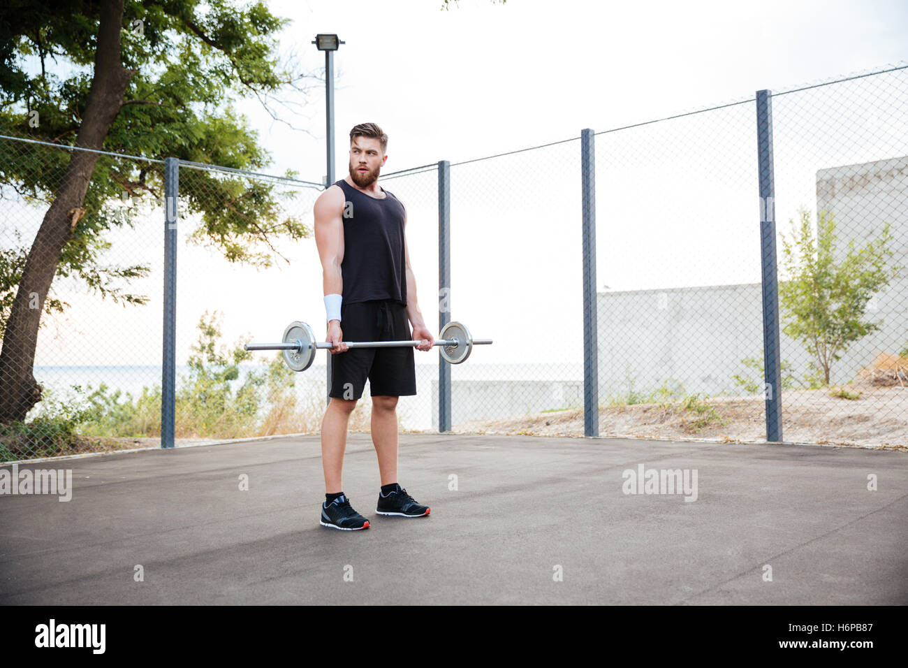 Full length of concentrated young man athlete working out with barbell ...