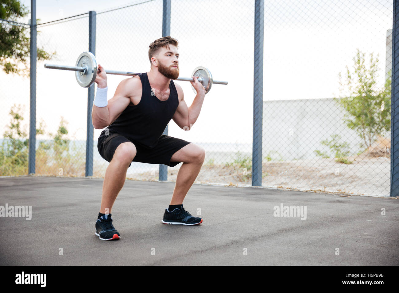 Concentrated bearded sports man doing squatting exercises with barbell ...