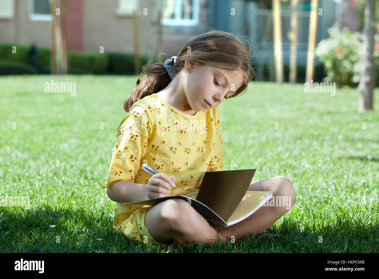 portrait of little girl studying on the grass in summer environment ...