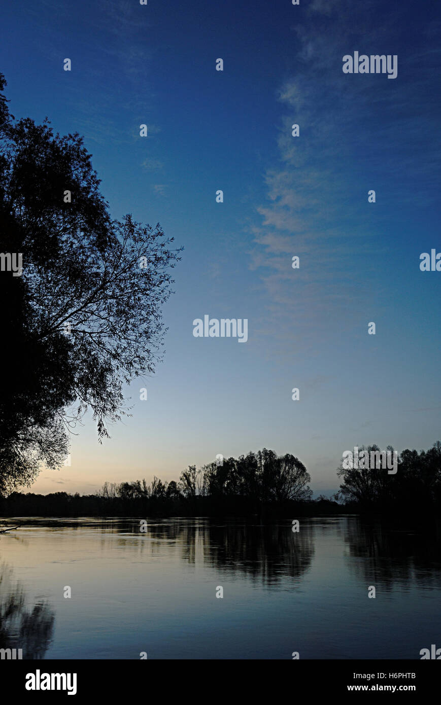 Night sky changing colors at dawn over water surface with dark trees on ...