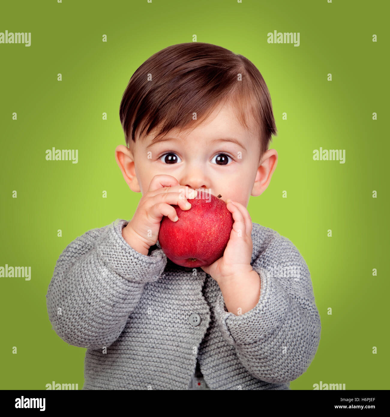 Adorable baby eating a red apple on a green background Stock Photo - Alamy