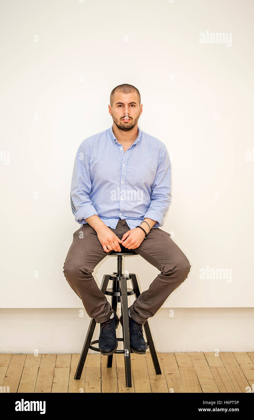 Man posing on the stool by the white wall Stock Photo - Alamy