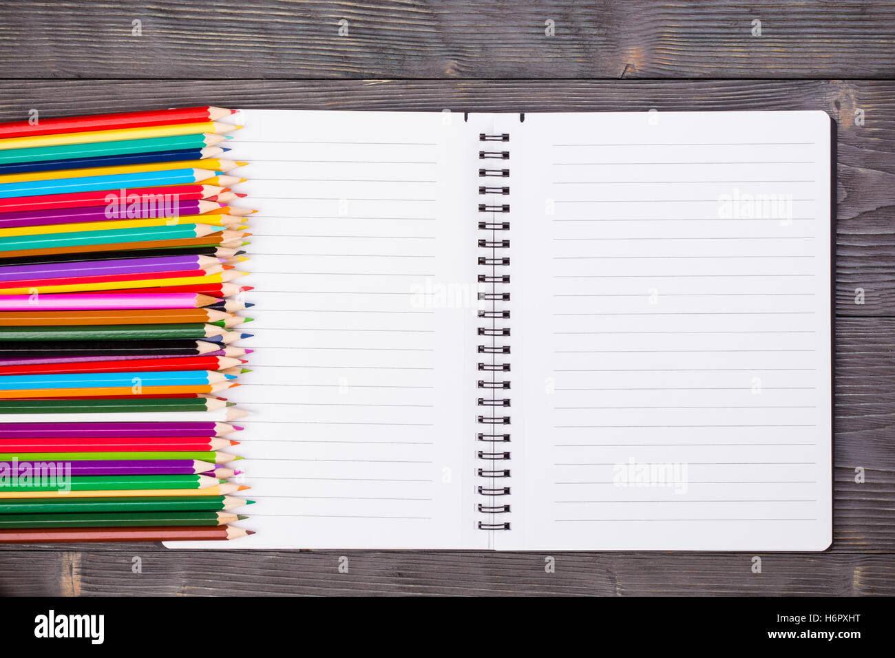 Bunch of color pencils and open notebook on gray wooden background ...